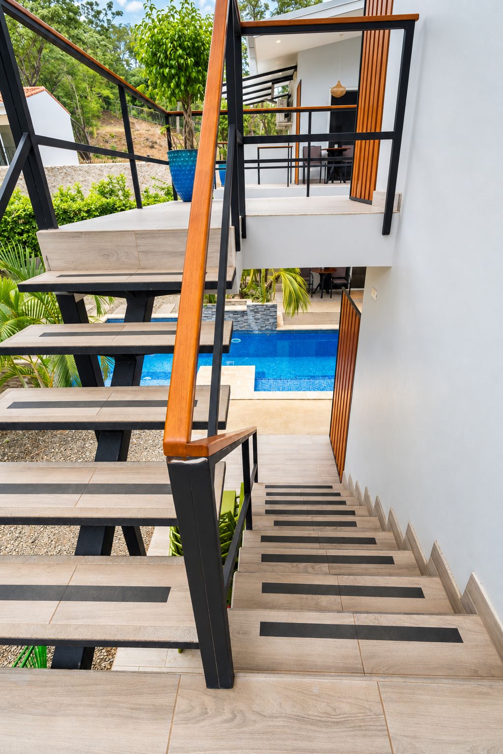 Uma escadaria moderna com degraus de madeira e corrimãos pretos que dá acesso a uma área de piscina.