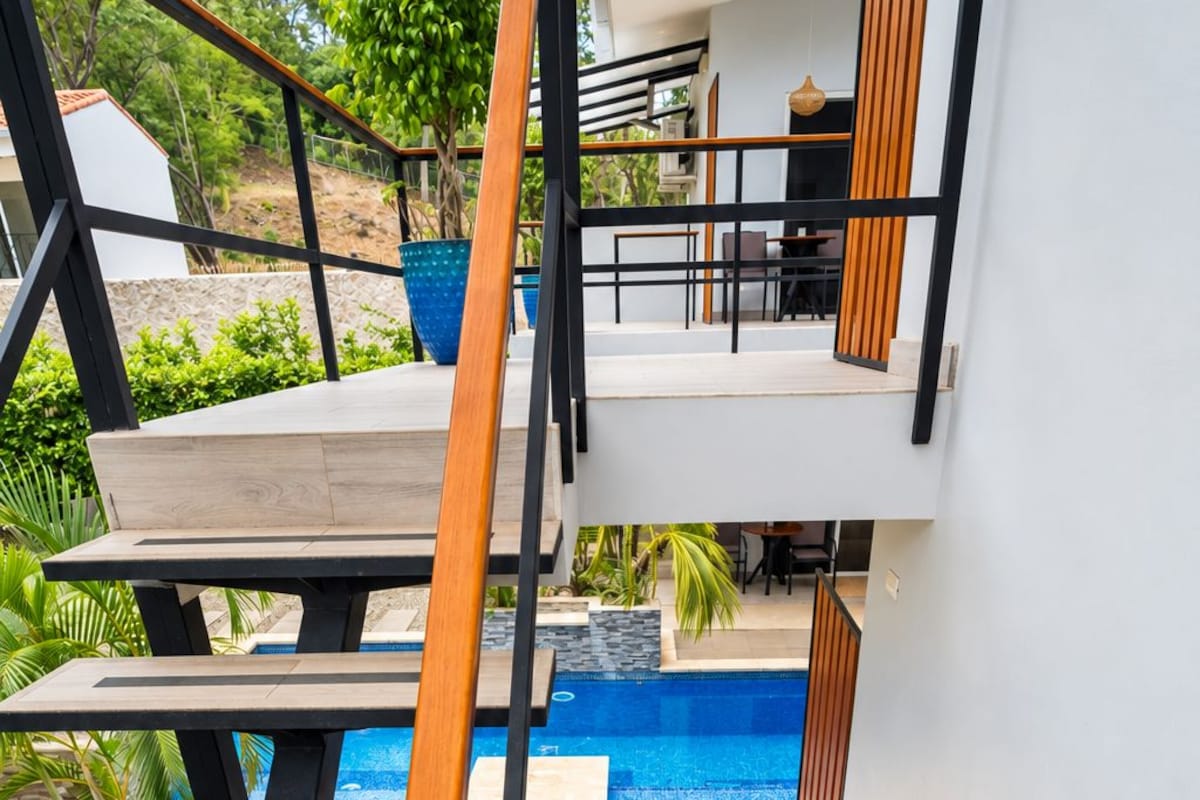 Uma escadaria moderna com degraus de madeira e corrimãos pretos que dá acesso a uma área de piscina.
