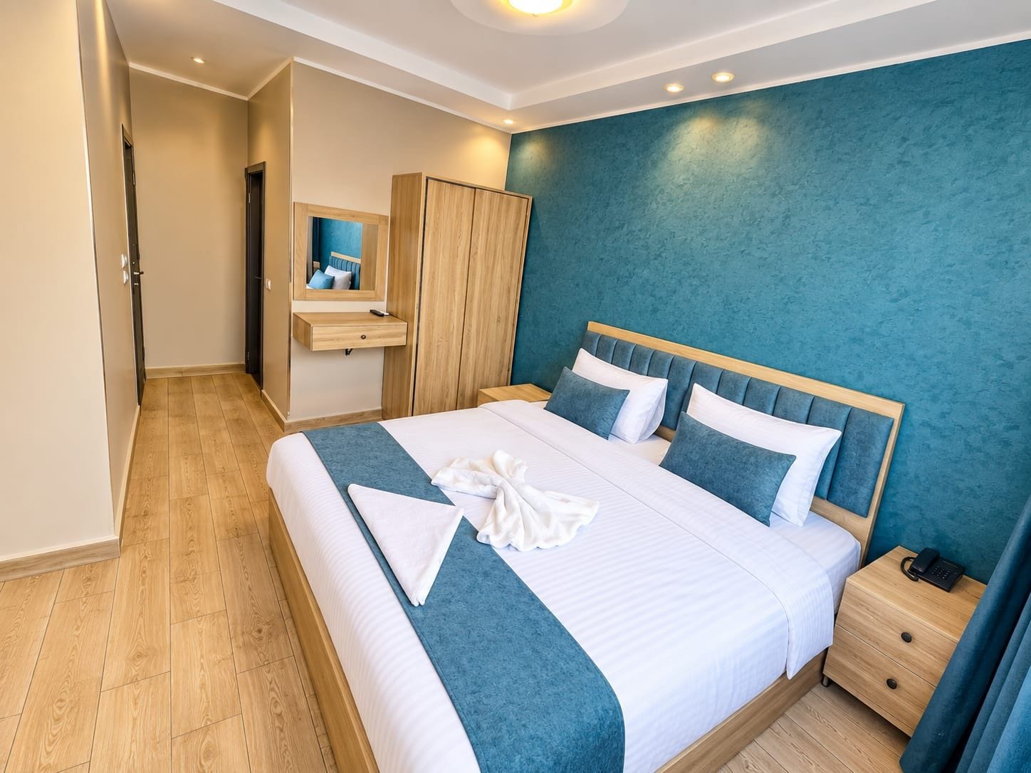Quarto de hotel com uma cama grande, um guarda-roupa de madeira, uma mesa de cabeceira com telefone e um banheiro com espelho e pia.