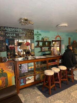 Uma área de bar com bancos, balcão e diversos objetos nas prateleiras.