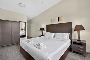 Quarto de hotel com uma cama grande, um guarda-roupa, uma mesa de cabeceira e um criado-mudo.