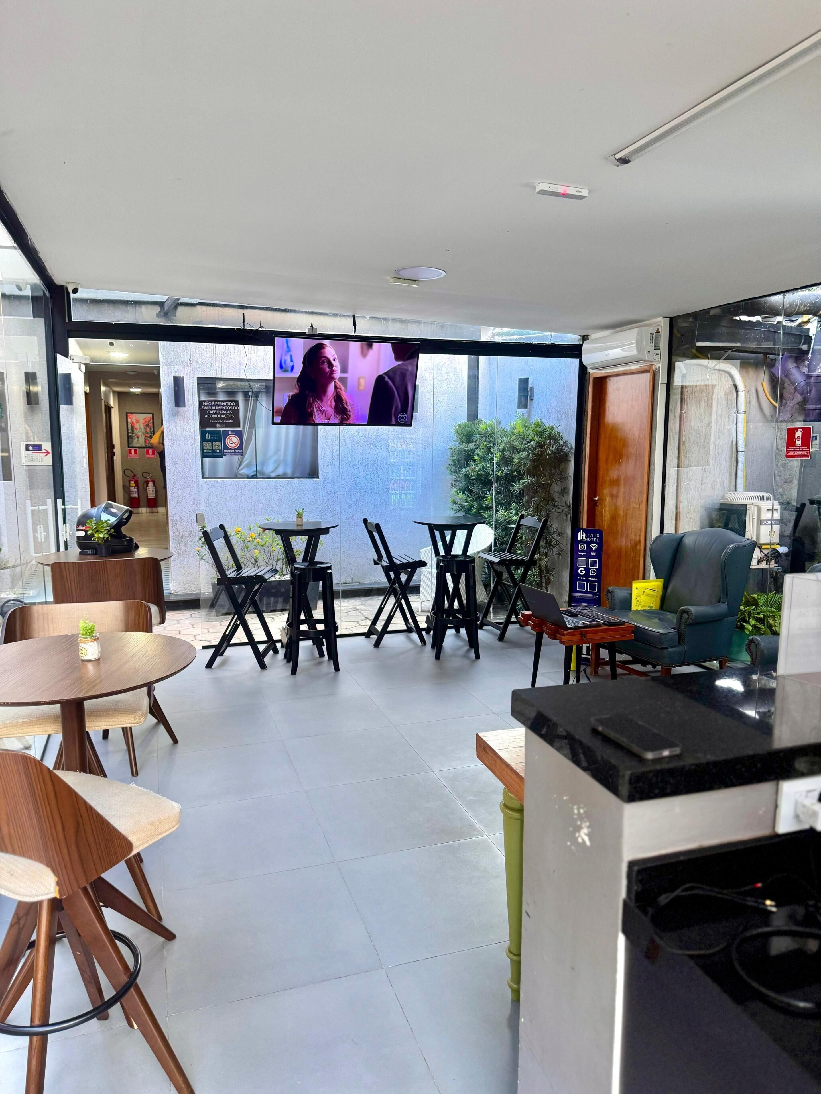 Um interior moderno com televisão de tela plana na parede, mesas e cadeiras de madeira, e uma área de estar com sofá e poltronas.