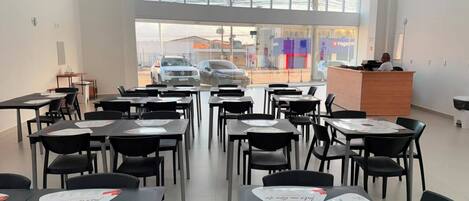 Uma sala de aula com mesas, cadeiras, um estrado e vista para o exterior.