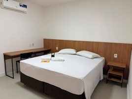 Quarto de hotel com uma cama, uma escrivaninha e uma cadeira.