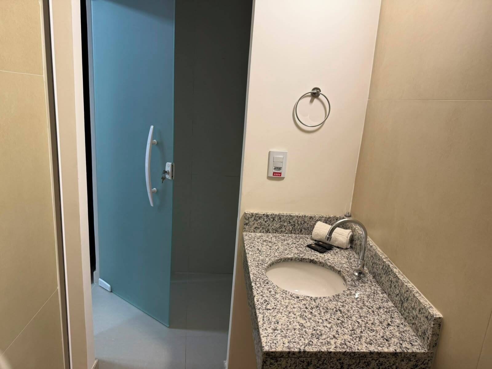Casa de banho com lavatório de bancada de granito, suporte de toalha e porta que dá para outro quarto.