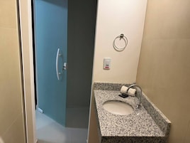 Casa de banho com lavatório de bancada de granito, suporte de toalha e porta que dá para outro quarto.
