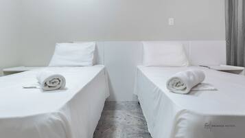 Quarto de hotel com duas camas de solteiro, cada uma com uma toalha branca enrolada. O quarto tem roupa de cama branca e chão de mármore.
