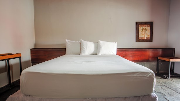 Quarto de hotel com uma cama grande, cabeceira de madeira, mesa de cabeceira e um quadro pendurado na parede.