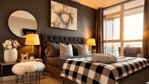 Um quarto moderno com cabeceira estofada, colcha xadrez e uma janela grande com cortinas.