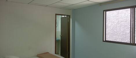 Um quarto com uma cama, janela com persianas, porta e luminária no teto.