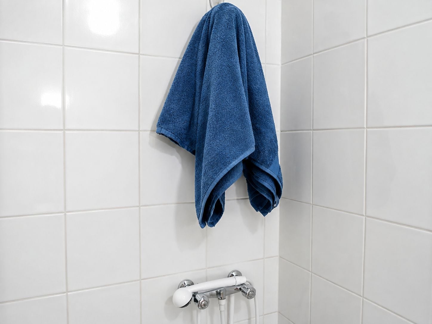 Casa de banho com azulejos brancos, um porta-toalhas com toalha azul e um chuveiro branco.