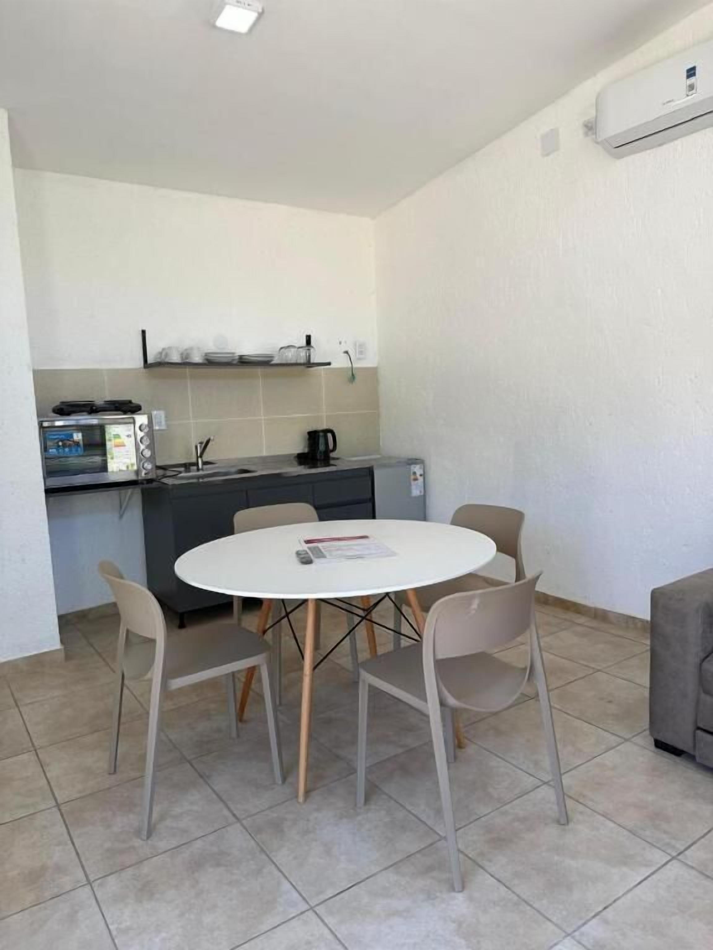 Cozinha compacta com área de refeições, incluindo uma mesa redonda e quatro cadeiras, uma cafeteira e um micro-ondas.
