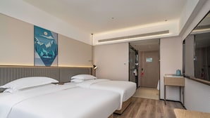 Quarto de hotel com duas camas, banheiro com espelho e uma obra de arte pendurada na parede.
