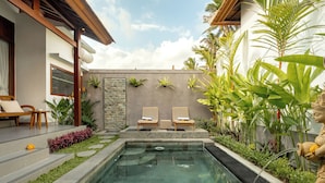 Uma piscina com duas espreguiçadeiras, rodeada por plantas tropicais e um muro de pedra.