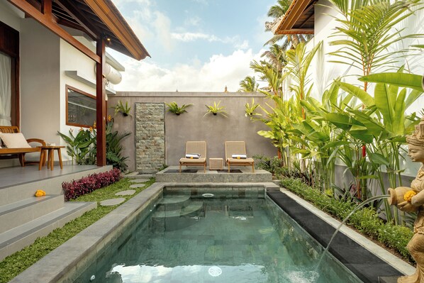Uma piscina com duas espreguiçadeiras, rodeada por plantas tropicais e um muro de pedra.