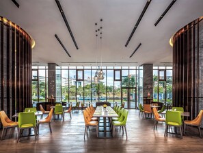 Uma sala de jantar ampla, com pé direito alto e grandes janelas, proporcionando vista dos edifícios e áreas verdes ao redor.
