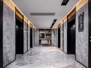 Um hall de elevadores moderno, com paredes e pisos de mármore, um balcão de recepção central e sinalização digital para elevadores.