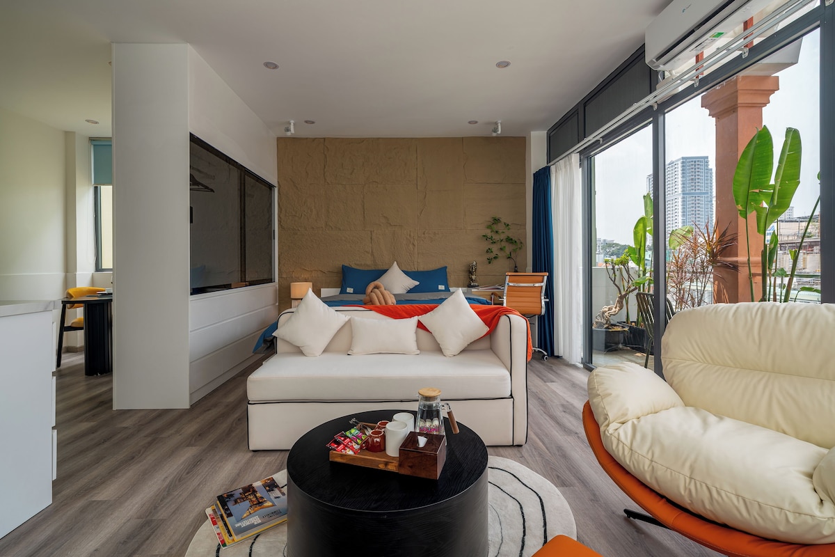 Quarto de hotel moderno com uma cama grande, um sofá, uma mesa de centro e vista para a cidade.