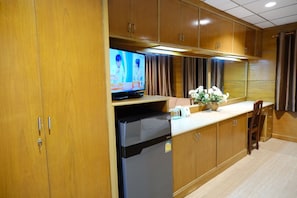 Uma cozinha compacta com armários de madeira, uma geladeira, uma televisão e um pequeno espaço de refeições com uma cadeira e um vaso de flores.