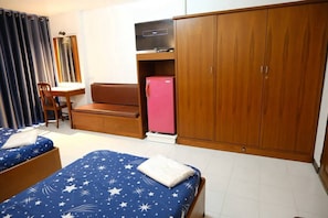 Quarto compacto com duas camas, uma escrivaninha, uma cadeira, um guarda-roupa e um frigorífico.