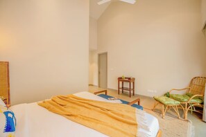 Um quarto com cama, uma cadeira, uma mesinha e uma porta.