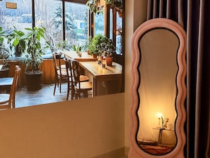 Uma área de refeições com mesa e cadeiras de madeira, plantas em vasos e vista para uma paisagem nevada através de grandes janelas.
