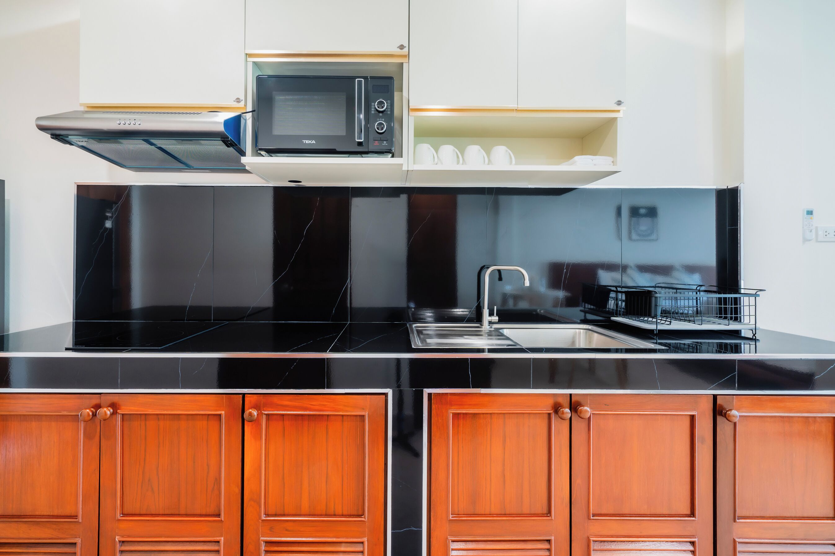 Uma cozinha moderna com bancadas pretas, armários de madeira, micro-ondas e pia.