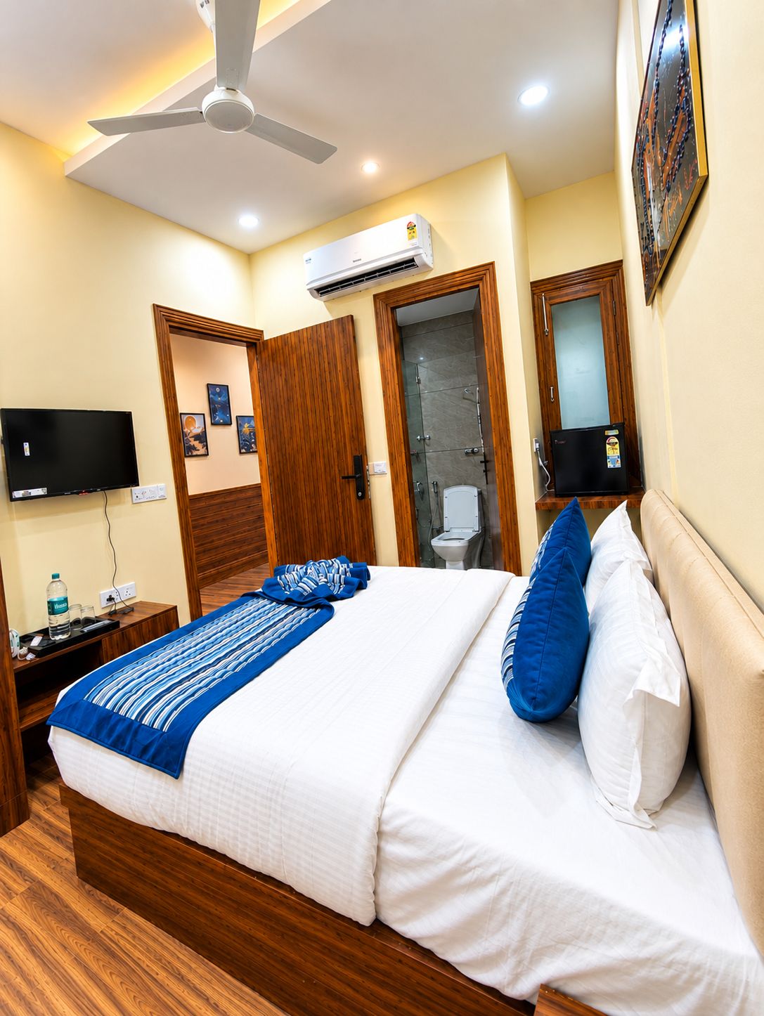 Quarto de hotel com cama, televisão, ar condicionado, chuveiro e porta.