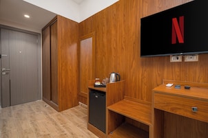 Quarto de hotel com guarda-roupa de madeira, uma kitchenette compacta, televisão de ecrã plano na parede e soalho em madeira.