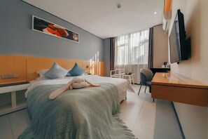 Quarto de hotel moderno com cama, escrivaninha, cadeira e televisão.