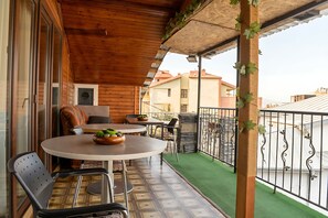 Varanda de madeira com mesa e cadeiras, um pequeno jardim e vista para edifícios vizinhos.