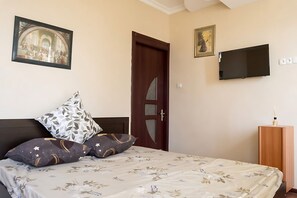 Quarto com uma cama, duas almofadas, uma televisão e uma porta.