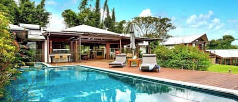 Piscina com espreguiçadeiras, um alpendre coberto e vista para uma casa com terraço.