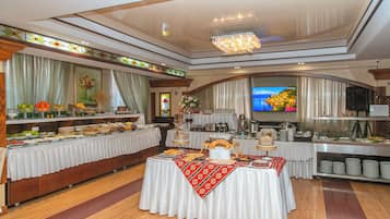 Disposição de buffet com diversos alimentos e uma tela de televisão ao fundo.