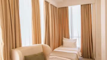 Quarto de hotel com uma cama de solteiro, uma cadeira e cortinas.