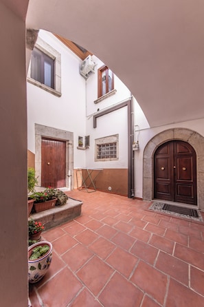Um pátio com telhas de terracota, uma porta de madeira e um arco de pedra.