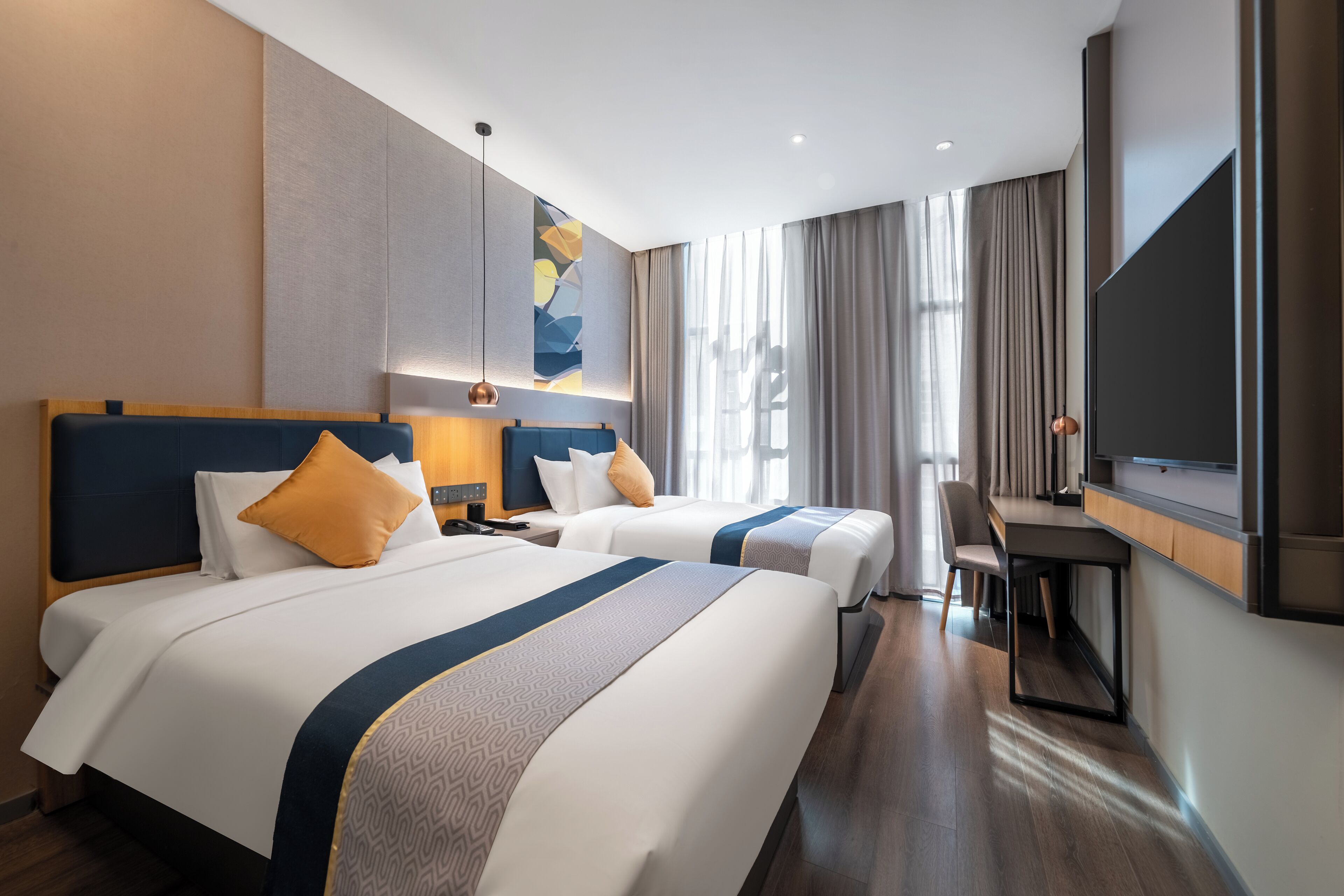 Quarto de hotel com duas camas, uma escrivaninha, televisão e uma janela grande com cortinas.