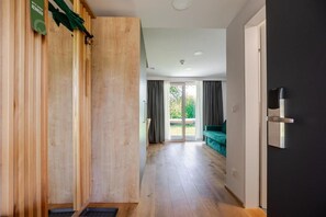 Um corredor com painéis de madeira, uma porta deslizante e vista para uma sala com um sofá verde e uma janela.