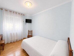 Um quarto com uma cama, uma cadeira, televisão na parede e uma janela com cortinas.