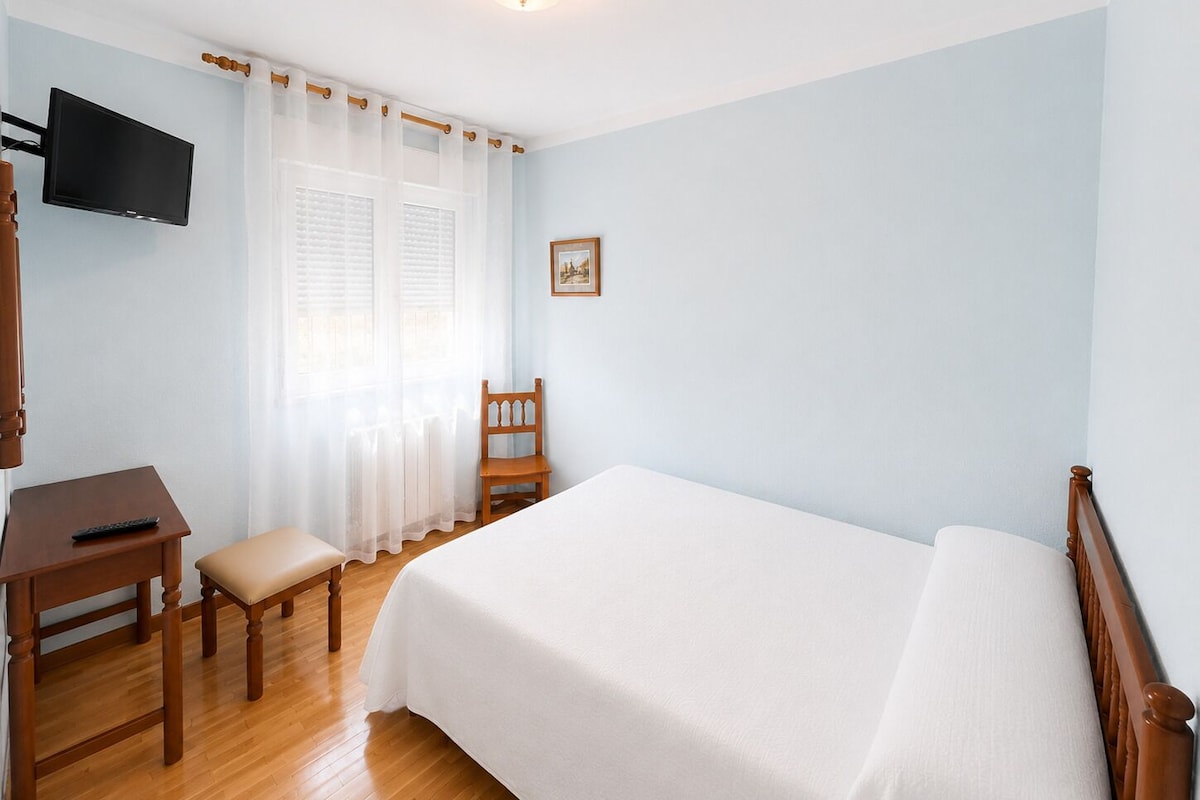 Quarto com cama, escrivaninha, cadeira, televisão e um quadro na parede.