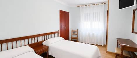 Quarto de hotel com duas camas de solteiro, uma secretária de madeira, televisão e uma janela com cortinas.
