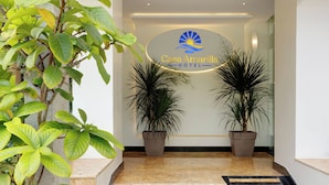 Uma área de recepção de hotel com uma placa indicando Casa Amarilla Hotel, duas plantas em vasos e uma escadaria de mármore.