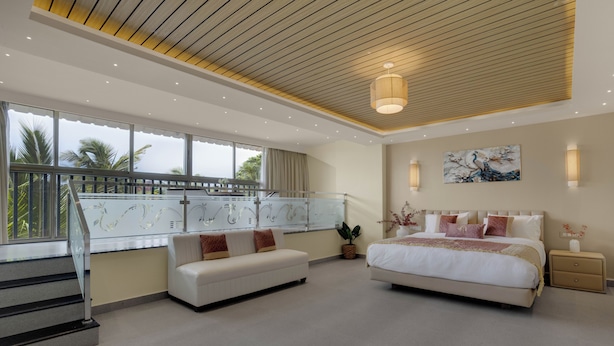Quarto moderno com cama, sofá, escada e uma grande janela com vista para palmeiras.