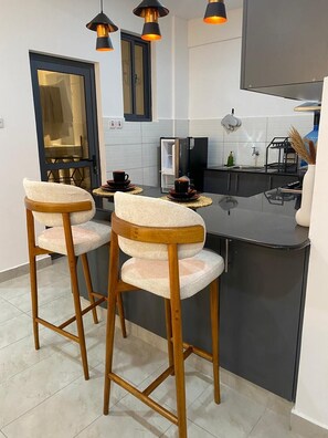 Uma cozinha moderna com bancada preta, banquetas de madeira e iluminação pendente.
