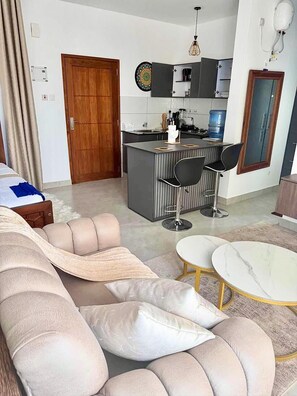 Uma sala de estar moderna com sofá, mesa redonda e área de cozinha com balcão e dois banquetes.