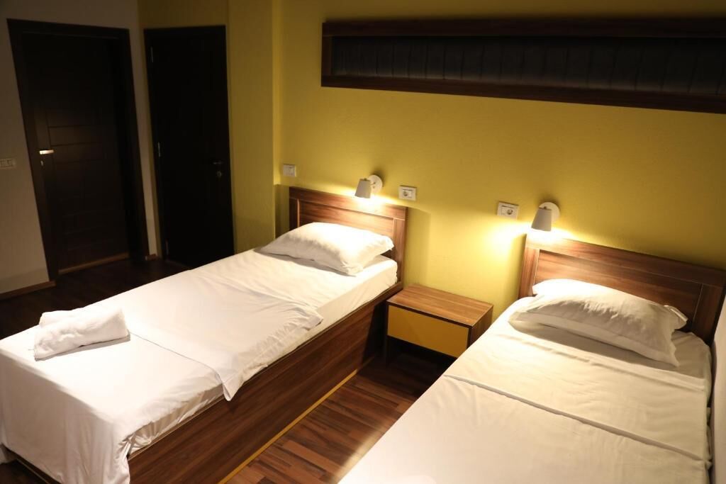 Quarto de hotel com duas camas de solteiro, piso de madeira e luminárias de cabeceira.