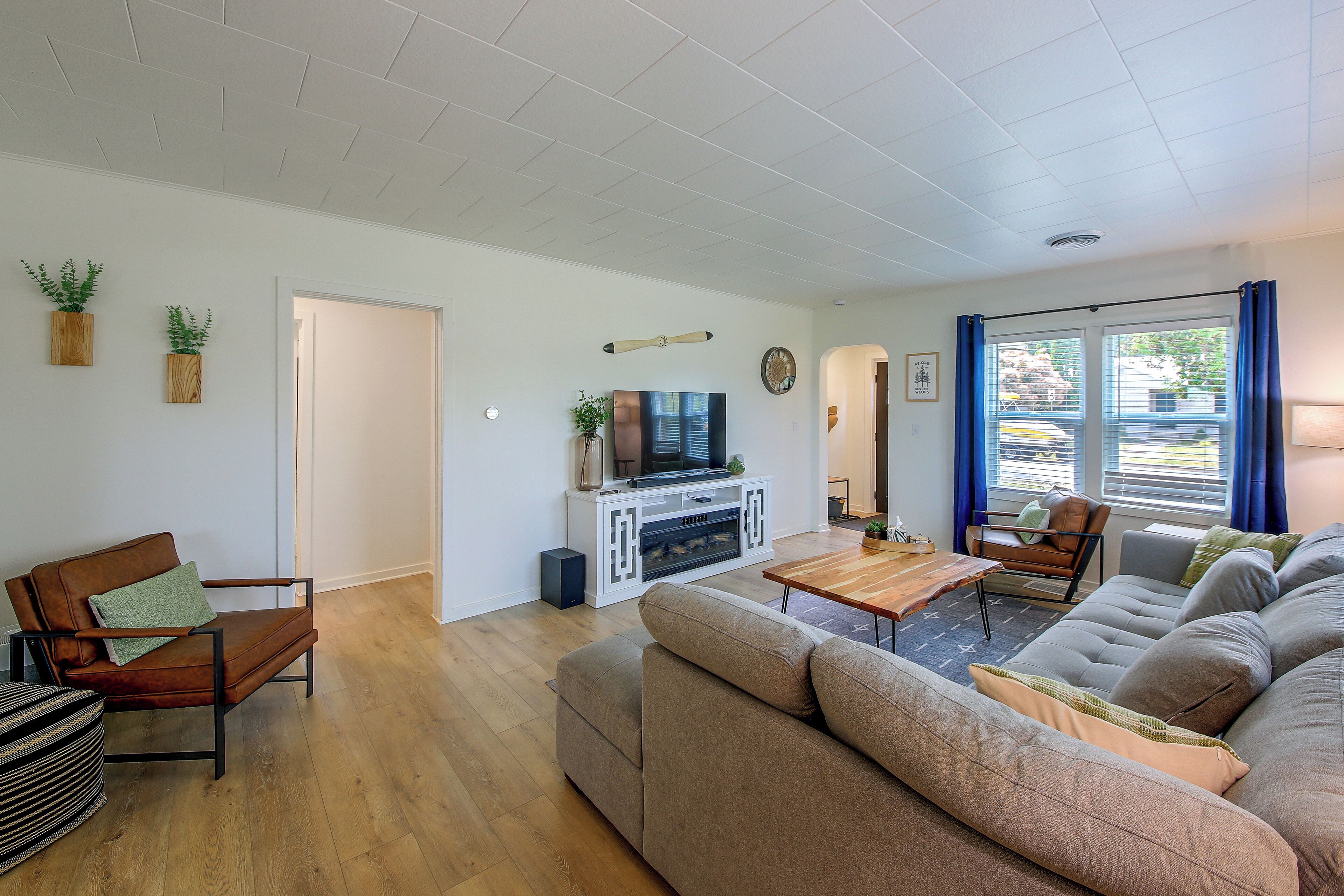 Uma sala de estar moderna com sofá, mesa de centro e televisão. Há dois armários de madeira e uma porta que dá para outro cômodo.