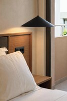 Quarto de hotel com uma cama, mesa de cabeceira, abajur e janela.