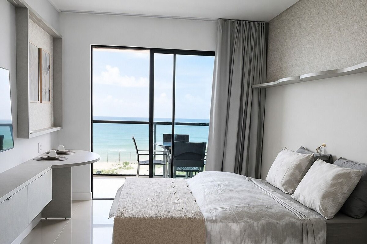 Quarto moderno com uma cama grande, uma escrivaninha e vista para o oceano.