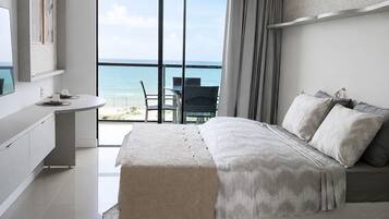 Quarto moderno com uma cama grande, uma escrivaninha e vista para o oceano.